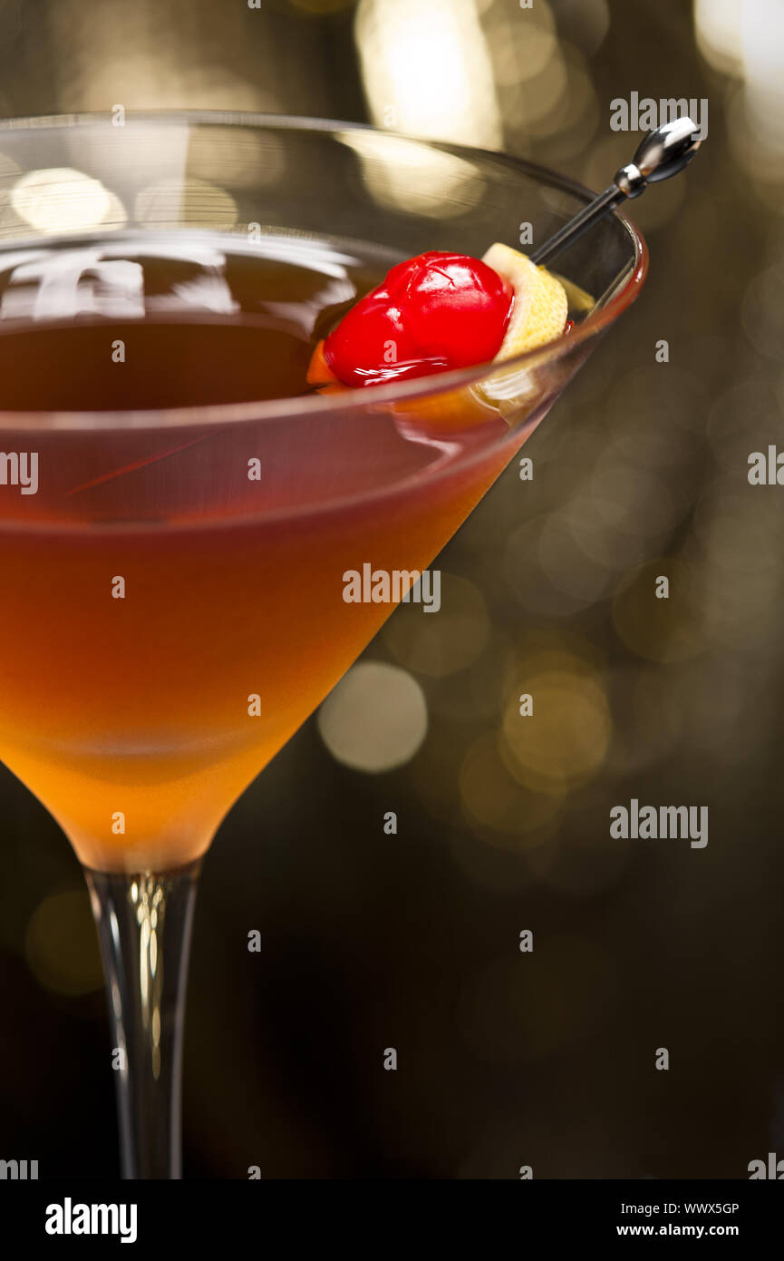 Manhattan cocktail garnished with a cherry and lemon and gold glitter ...