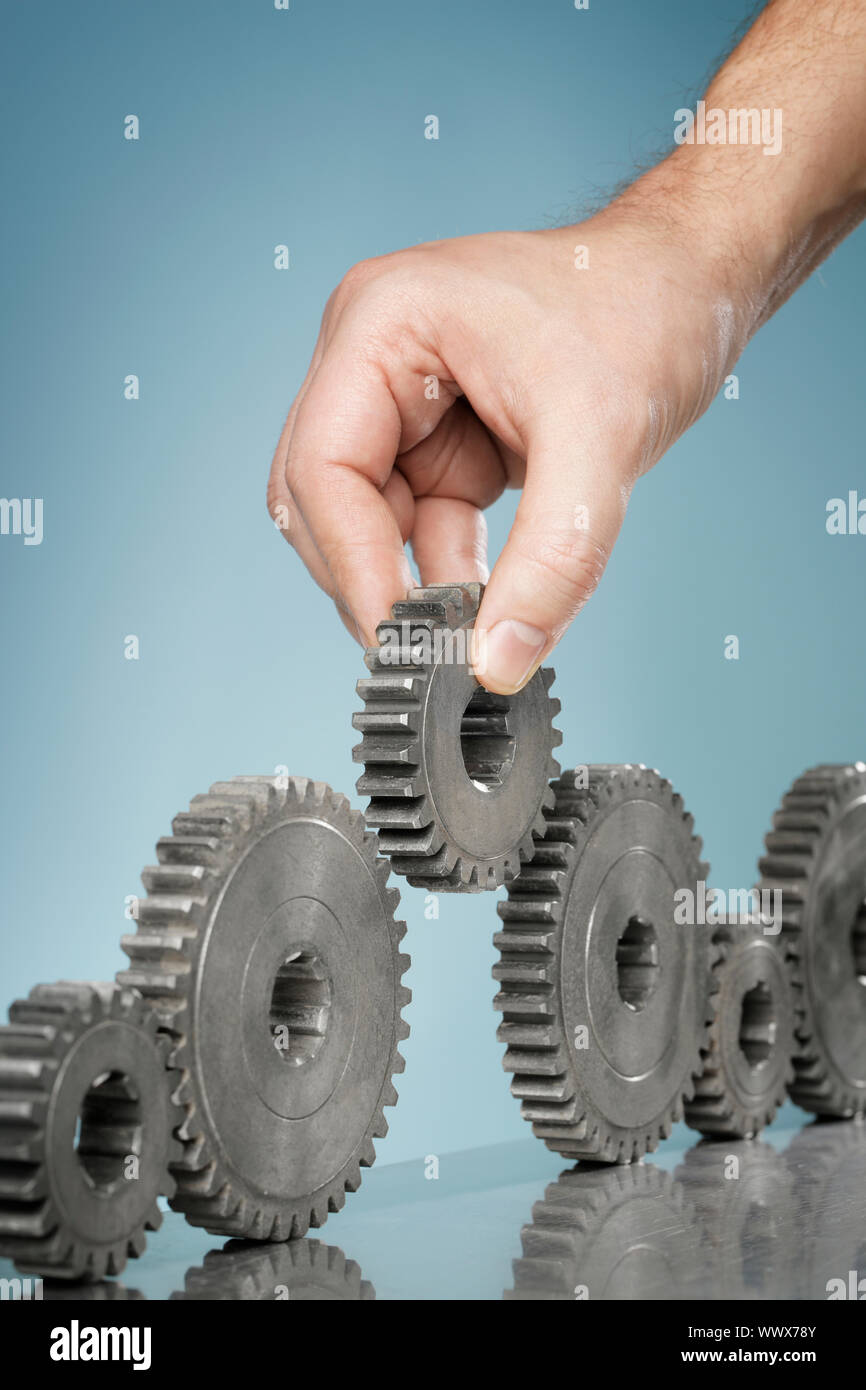 Man adding a cog gear wheel into a row of old cogs Stock Photo - Alamy