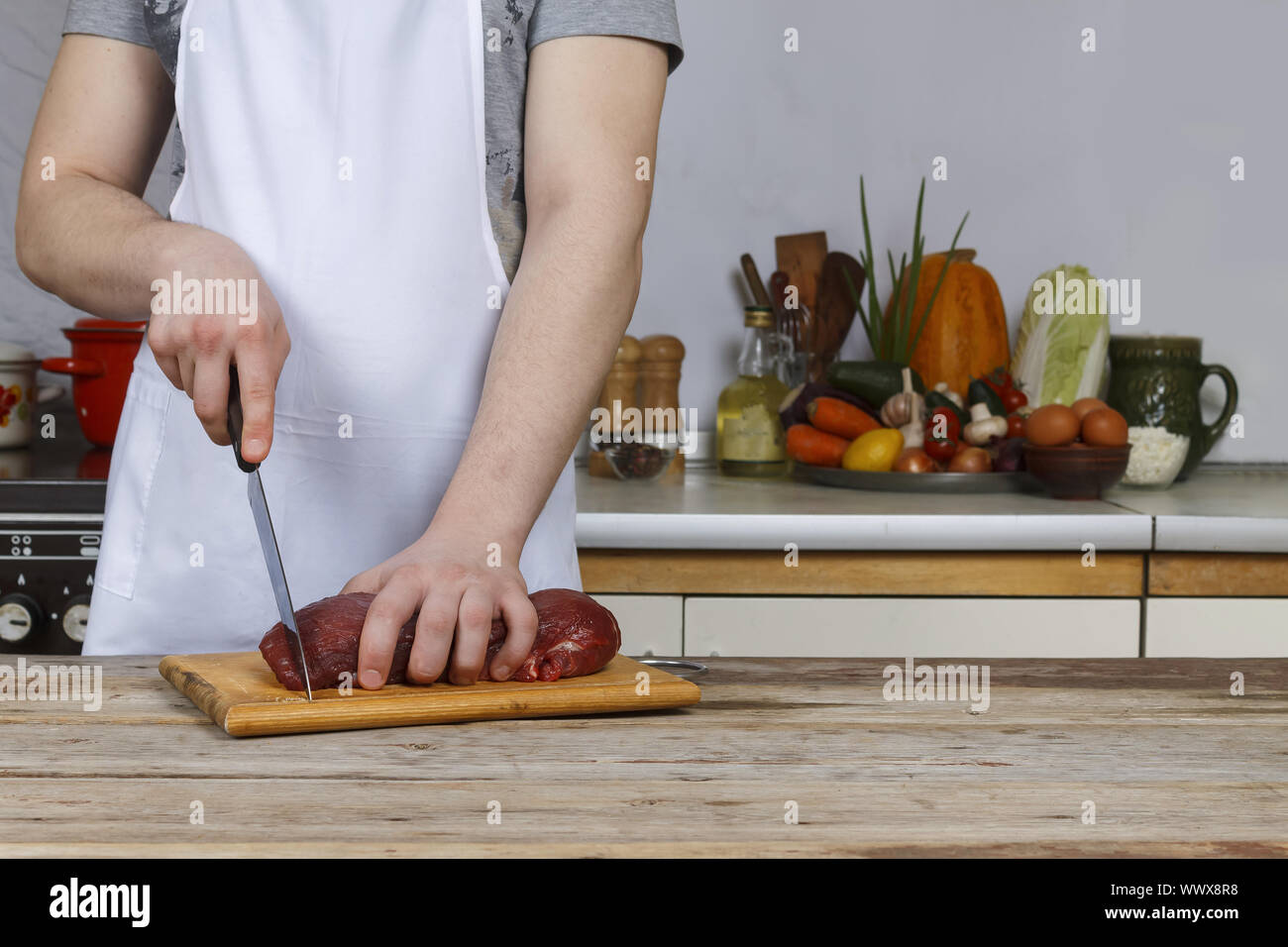 Man in the kitchen cutting a piece of meat Stock Photo - Alamy