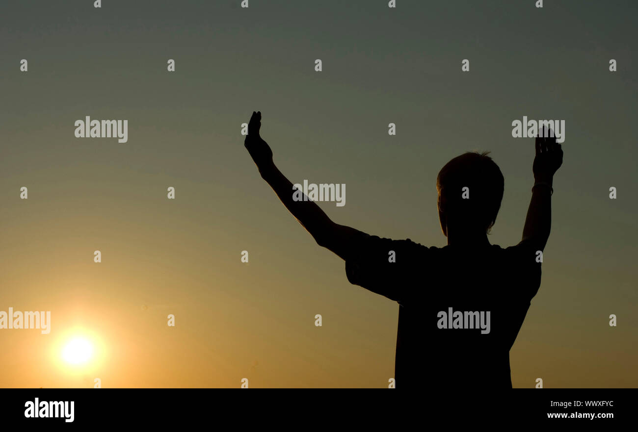 A man stands on against a sun with heaved up hands Stock Photo - Alamy
