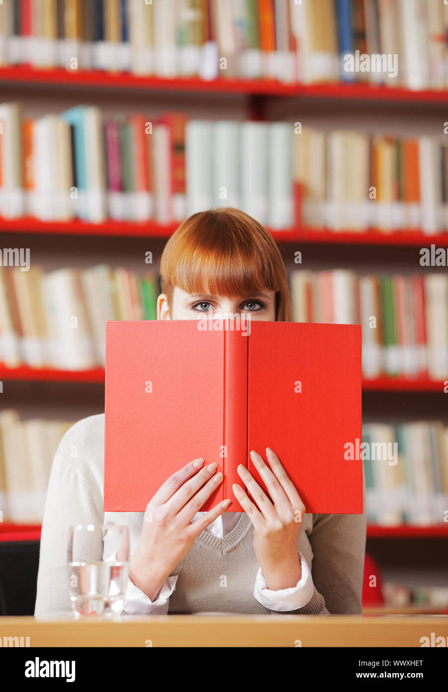 Girl hiding behind the book on library Stock Photo - Alamy