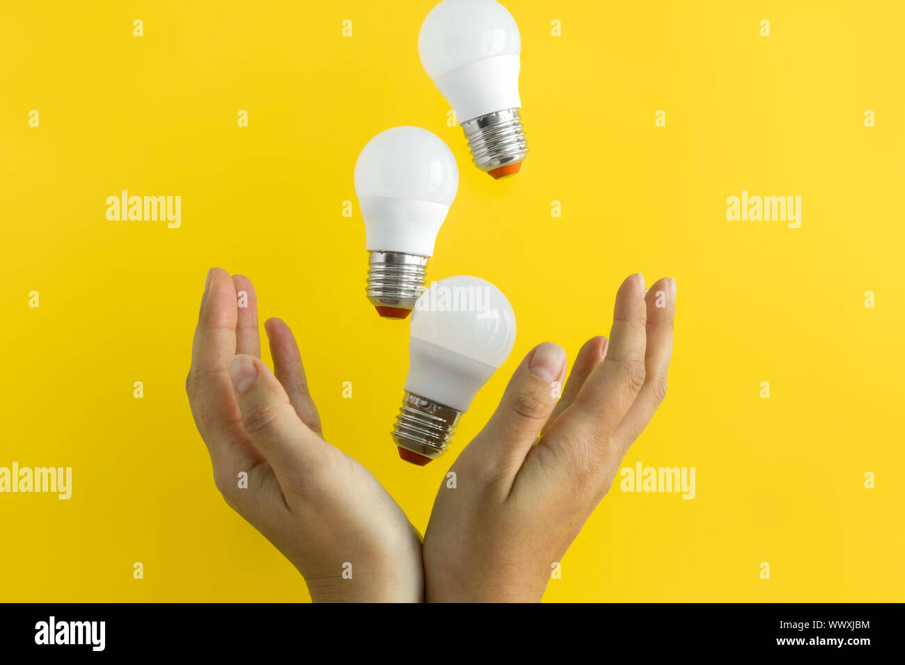 levitating energy saving light bulbs and female hands on a yellow ...
