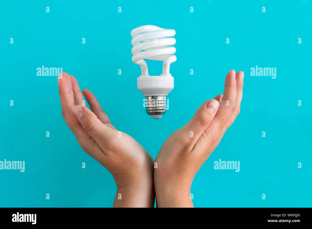 levitating spiral energy saving light bulb and female hands on blue ...