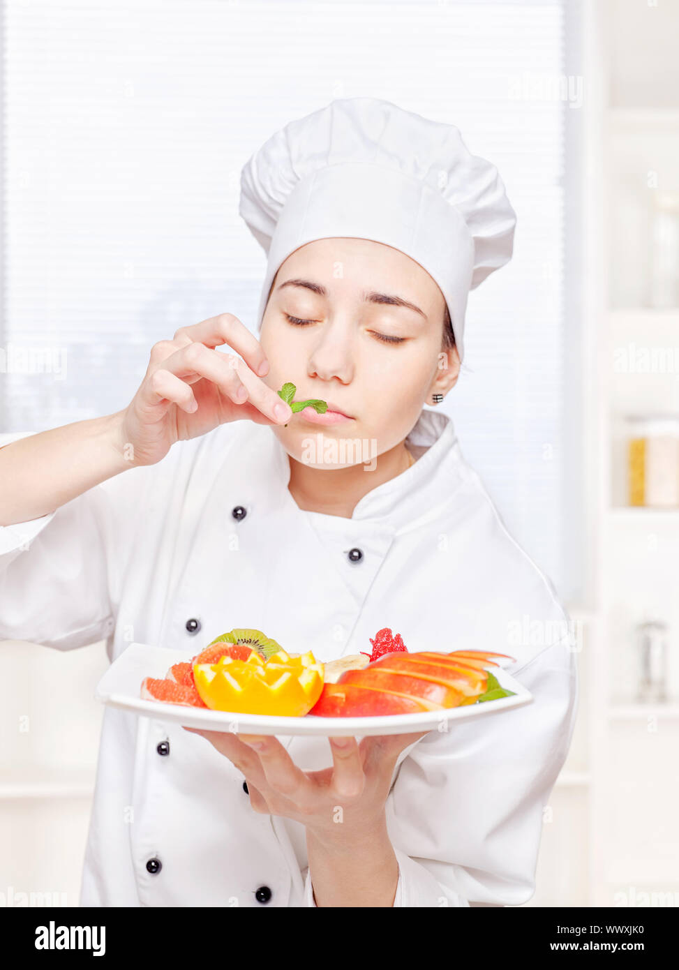 pretty young chef smell mint before putting it on a plate of fruit ...