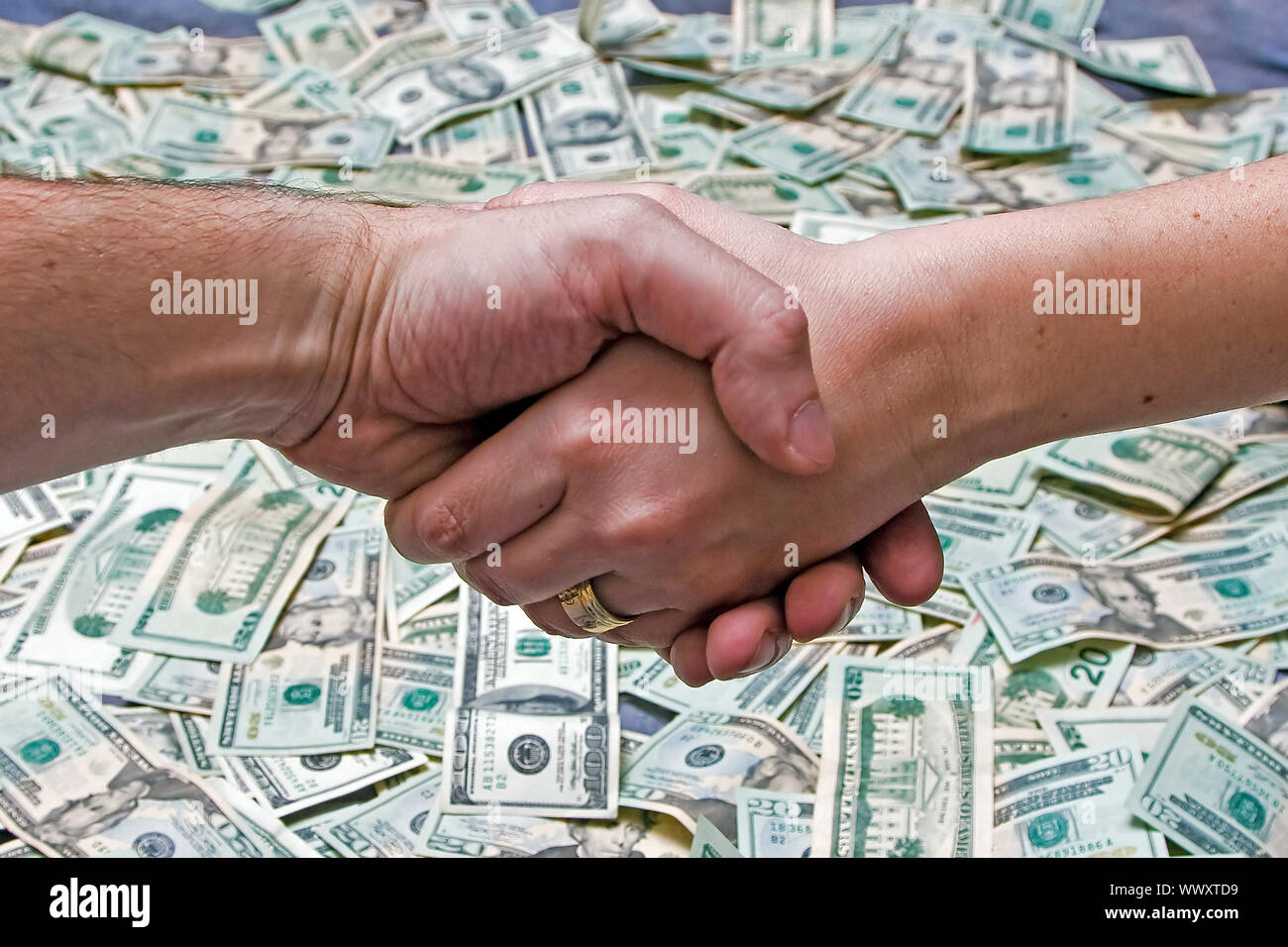Two shaking hands above a layer of lots of money Stock Photo - Alamy