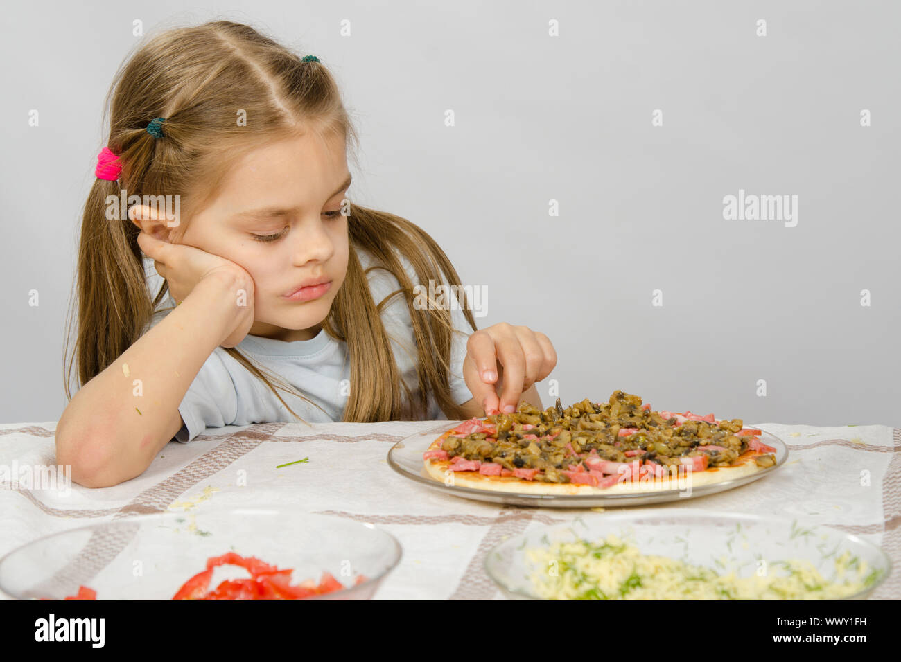 Little six year old girl sitting at the table and picks unfinished ...