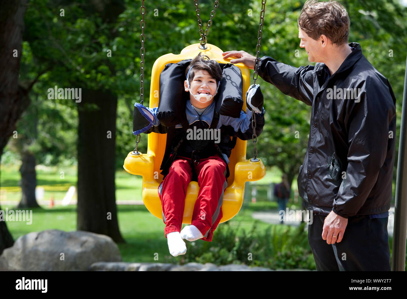 Father pushing disabled boy in special needs handicap swing. Child has ...