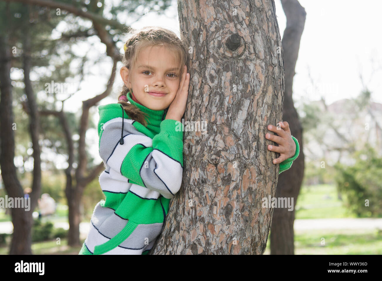 Joyful seven-year old girl sitting on a tree trunk in the early spring ...