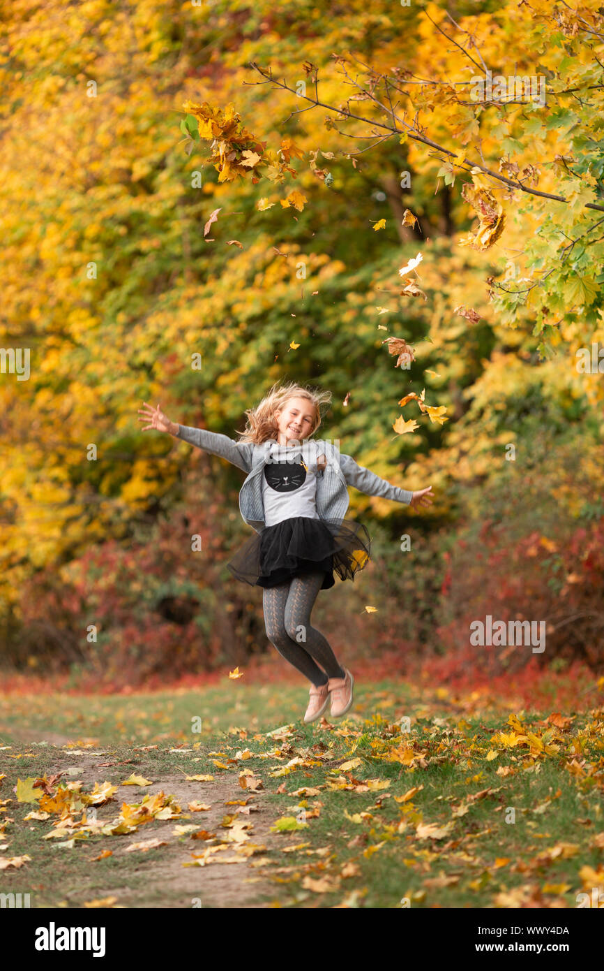 Beautiful little girl jumping with autumn leaves in the park outdoor ...