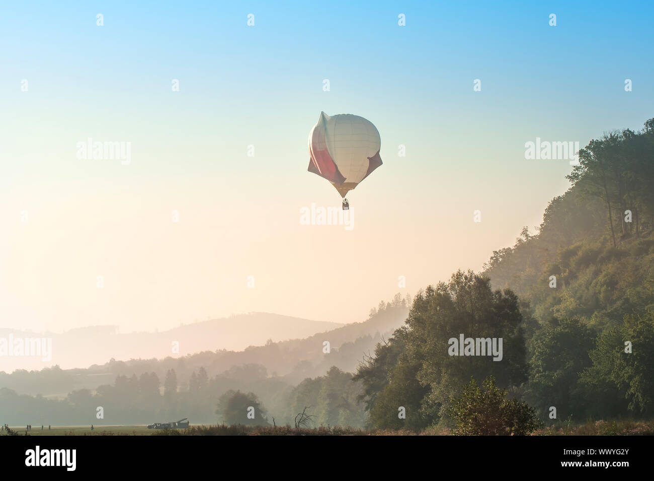 A hot air balloon starts its flight. It's early morning, the fog is ...