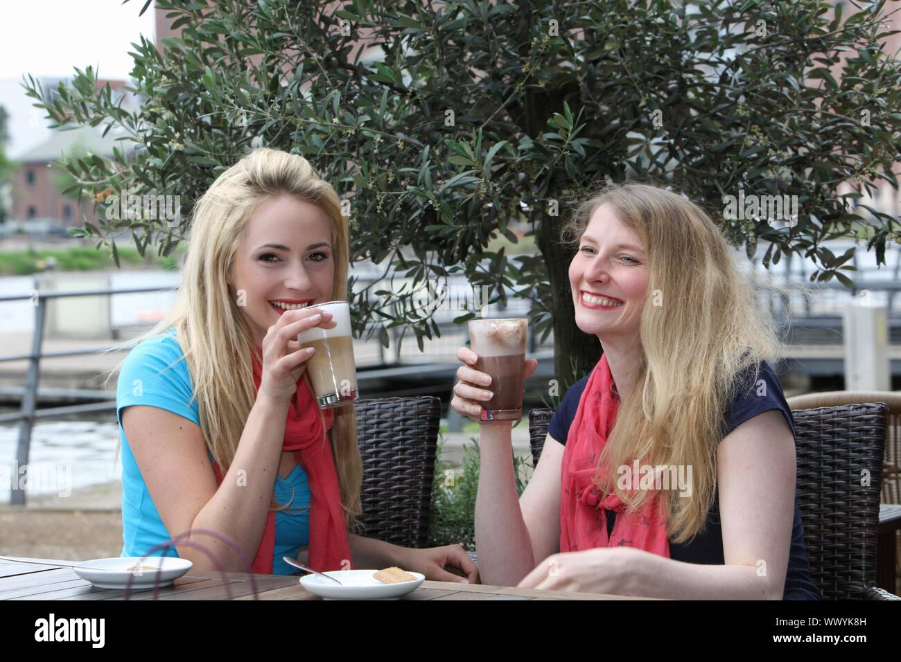 Laughing trendy woman relaxing over drinks seated at a table at an open ...