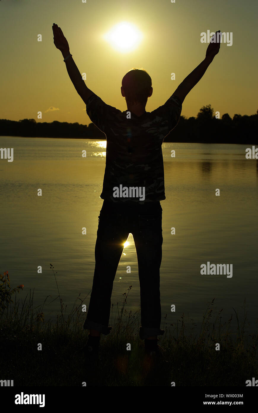 A man stands on against a sun with heaved up hands Stock Photo - Alamy