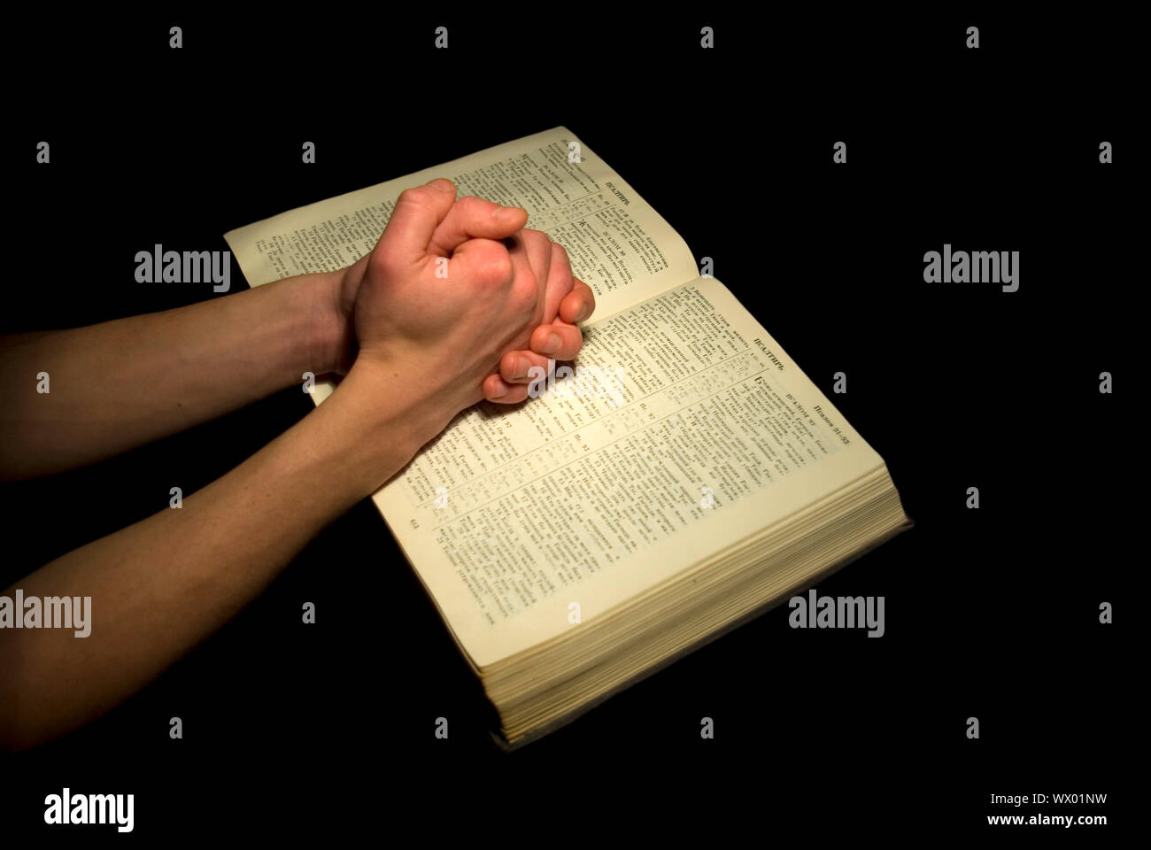 A mans hands clasped in prayer over a Bible Stock Photo - Alamy