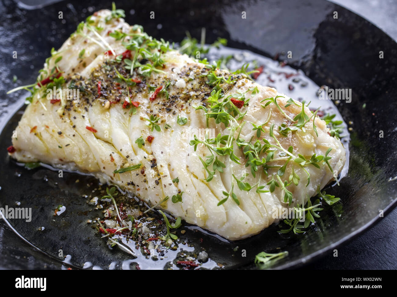 Fried cod fish fillet with spice and cress as close-up in a cast iron ...