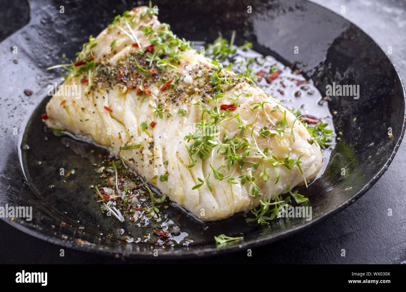 Fried cod fish fillet with spice and cress as close-up in a cast iron ...