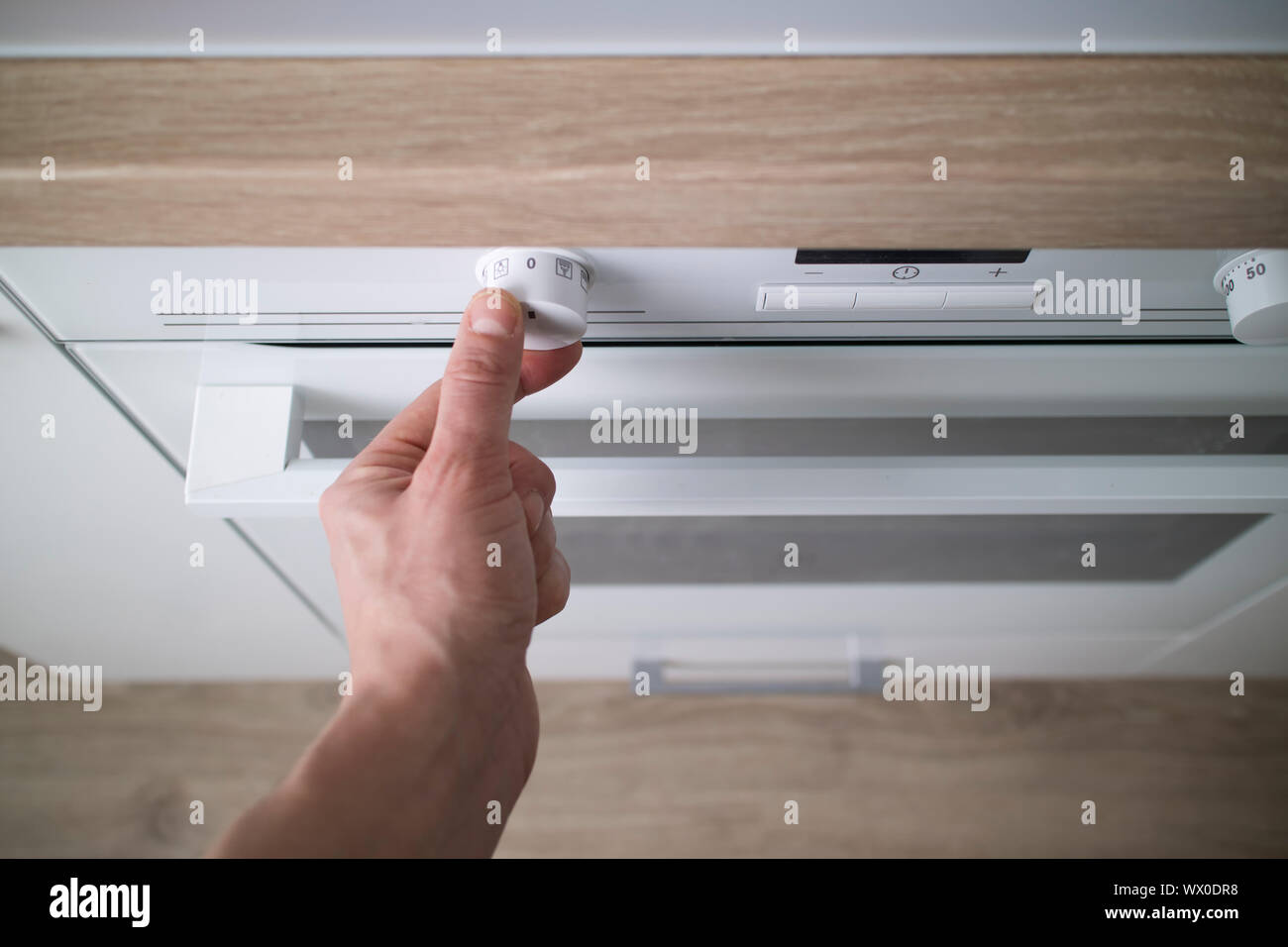 hand pushing a power button on a control panel of an electric oven ...