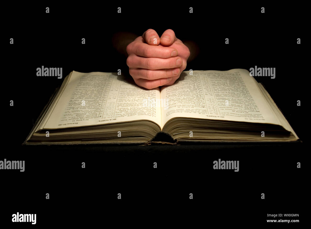 A mans hands clasped in prayer over a Bible Stock Photo - Alamy