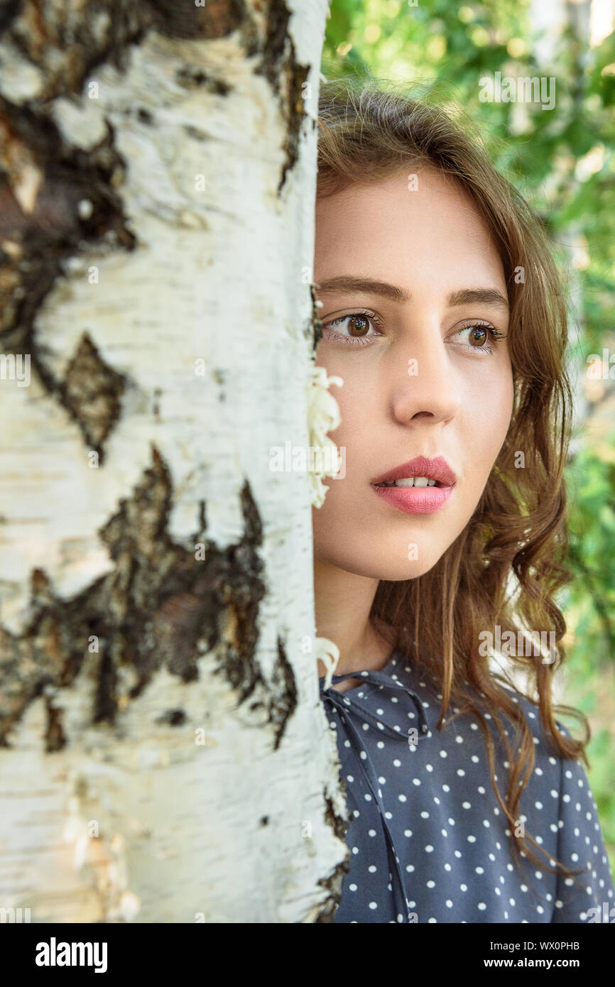 Portrait of Brunette girl behind the birch tree. Girl in blue dress ...