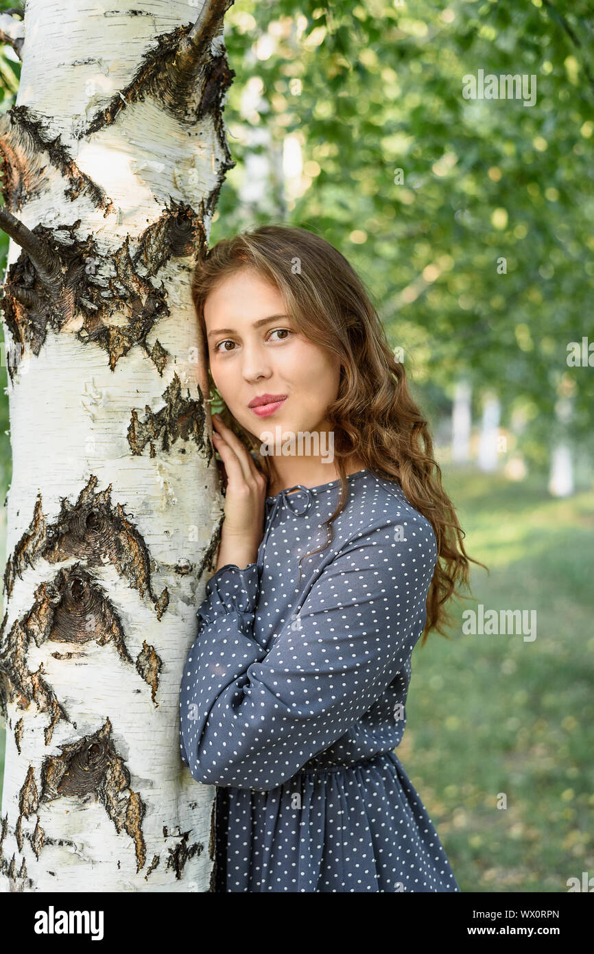 Portrait of Brunette girl behind the birch tree. Girl in blue dress ...