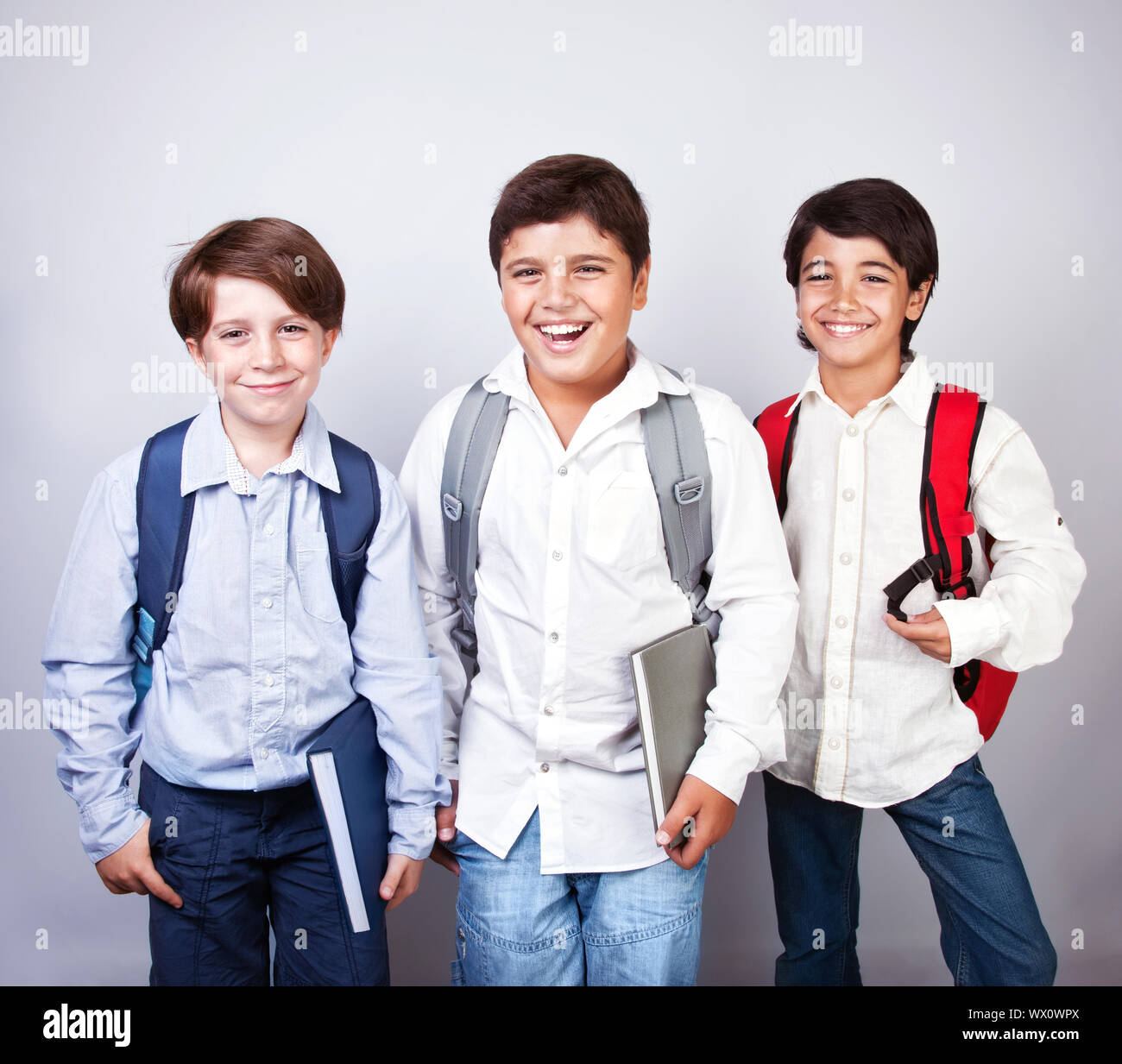 Three happy schoolboys isolated on gray&white background, back to ...