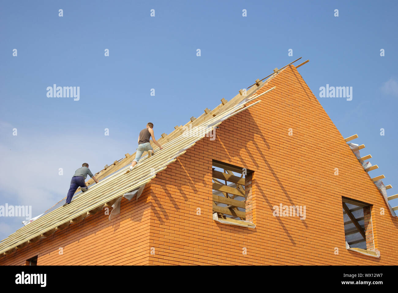 Construction workers placing the first section of roof on a new home ...