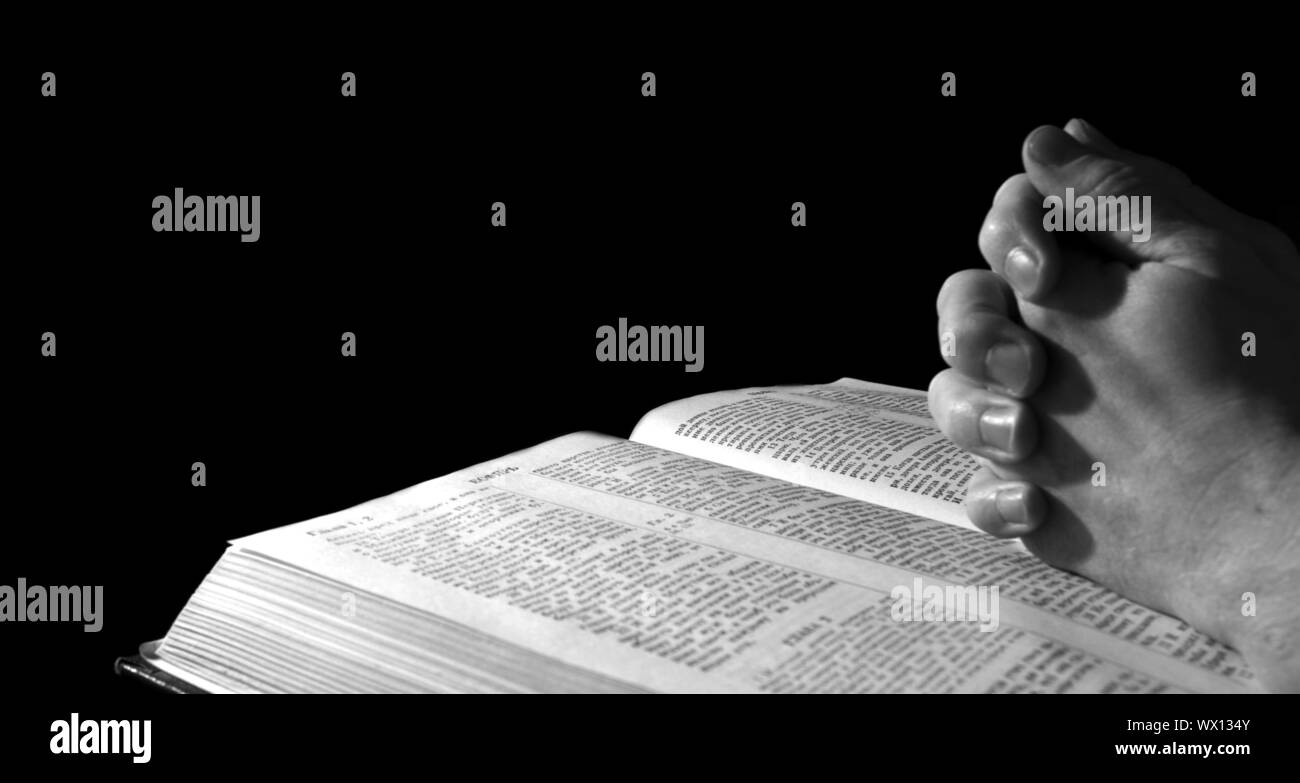 A mans hands clasped in prayer over a Bible Stock Photo - Alamy