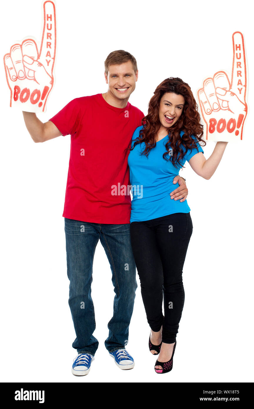 Excite young couple showing boo hurray foam hand and cheering against ...