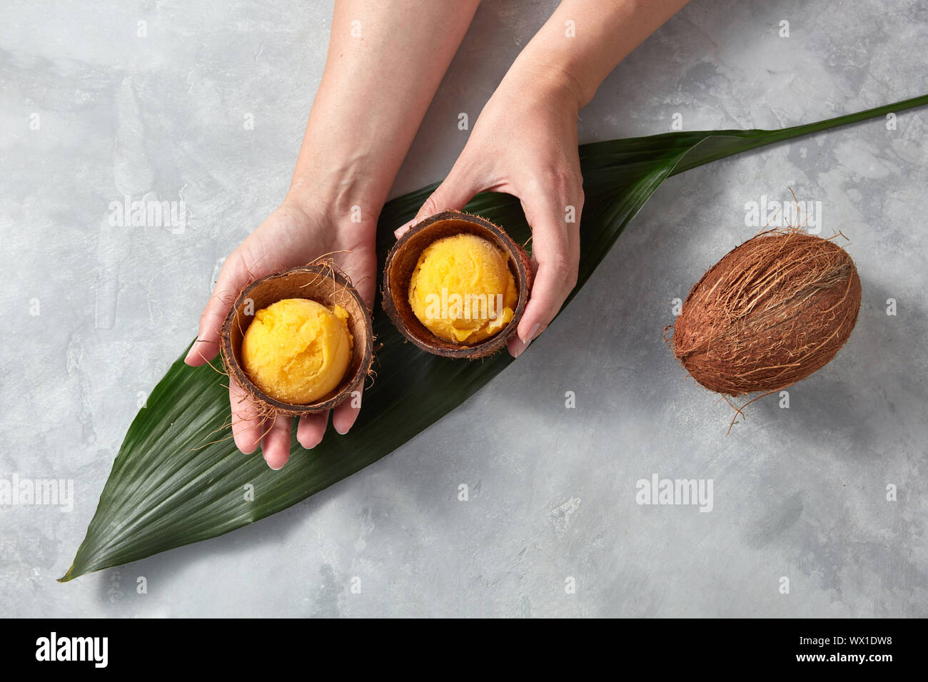 Female hands hold two halves of coconut shell with balls of yellow ...