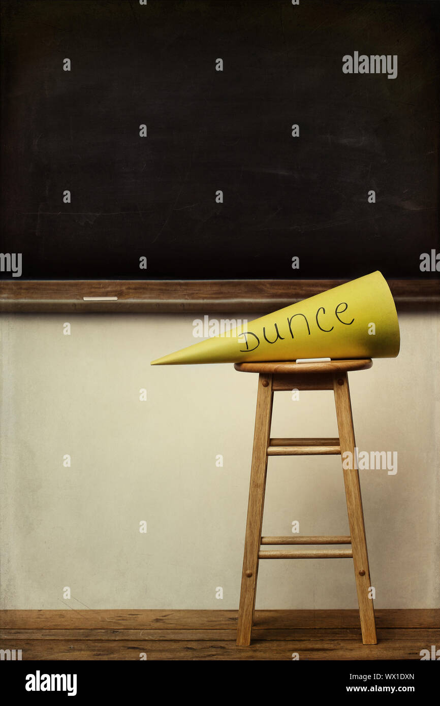 Yellow dunce hat on stool with chalkboard in background Stock Photo - Alamy