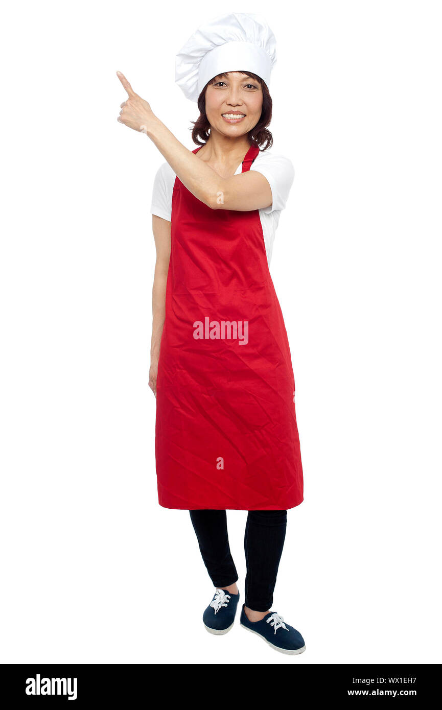 Beautiful female chef pointing at the copy space. Full length shot ...