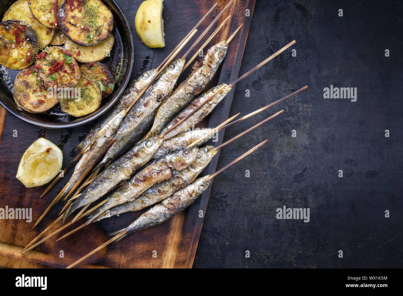 Traditional Spanish barbecue sardines on a wooden skewer with fries as ...
