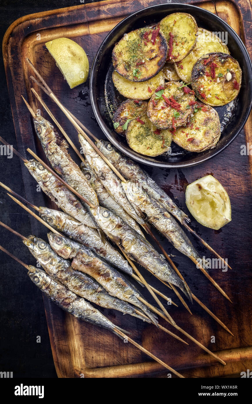 Traditional Spanish barbecue sardines on a wooden skewer with fries as ...