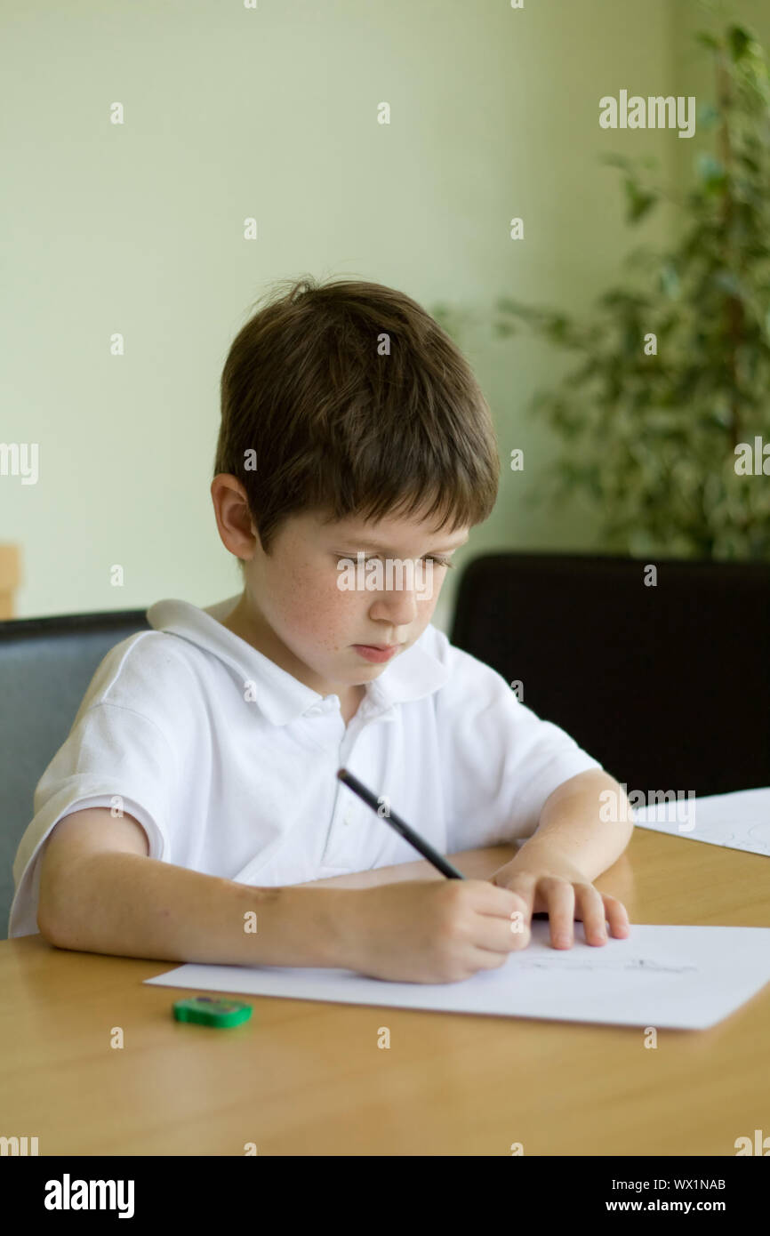 Boy at a table doing homework/drawing Stock Photo - Alamy