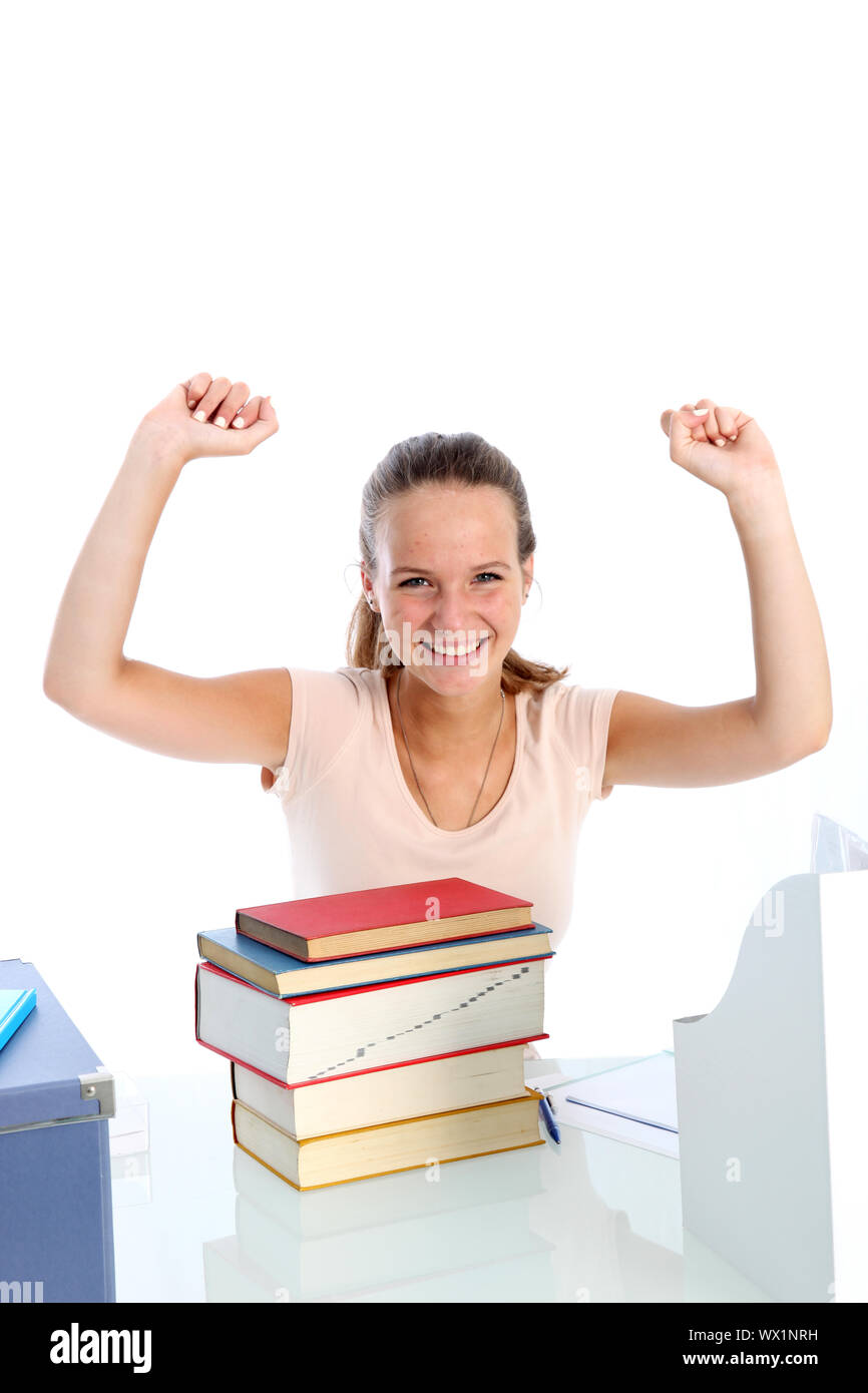 Jubilant young student sitting at her desk in front of a pile of ...