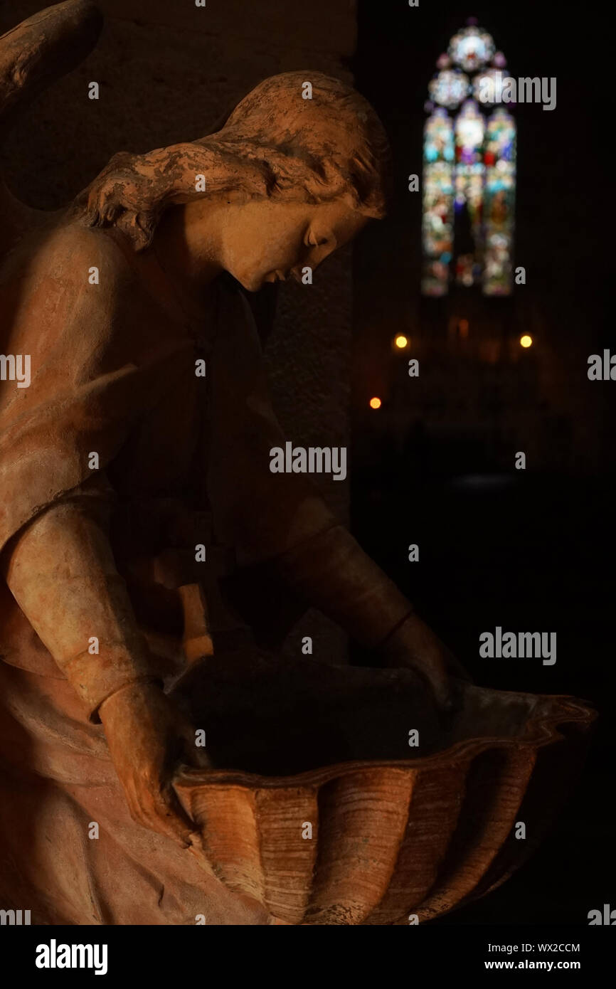 Religious statue font inside a church with stained glass window in ...
