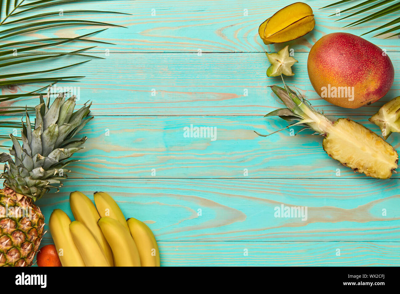 Corner frame from different tropical fruits and palm leaf on a blue ...