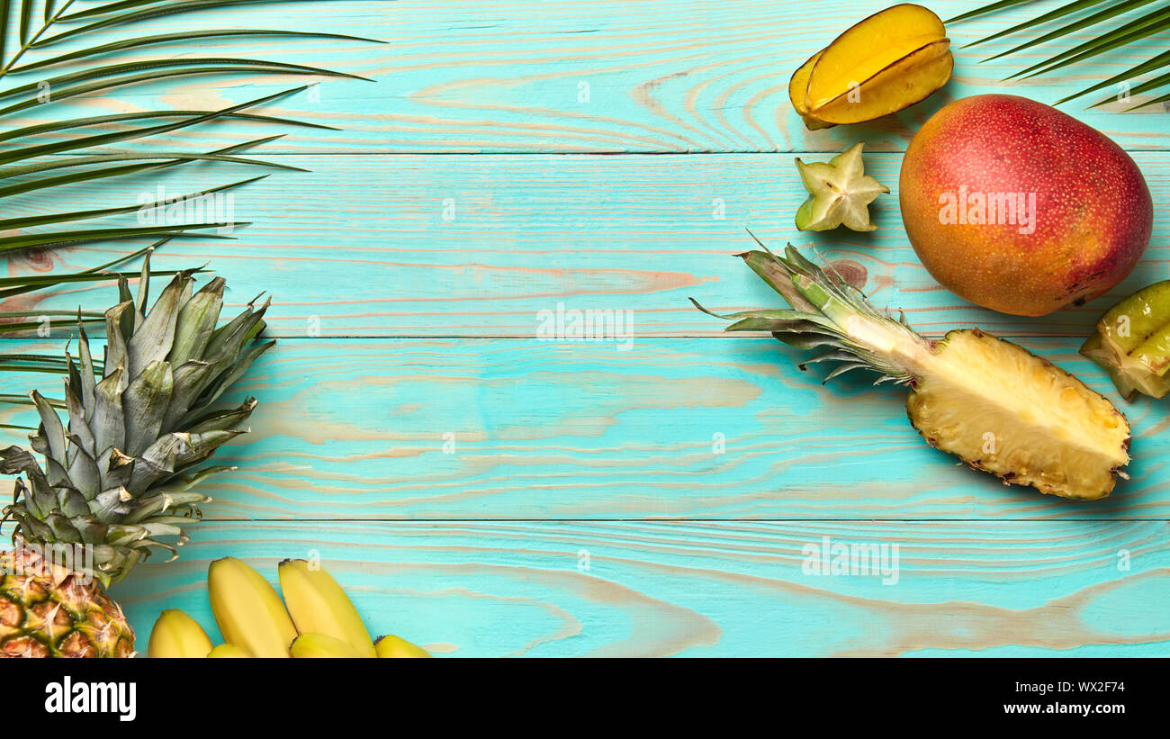Food frame from different tropical fruits and palm branches on blue ...