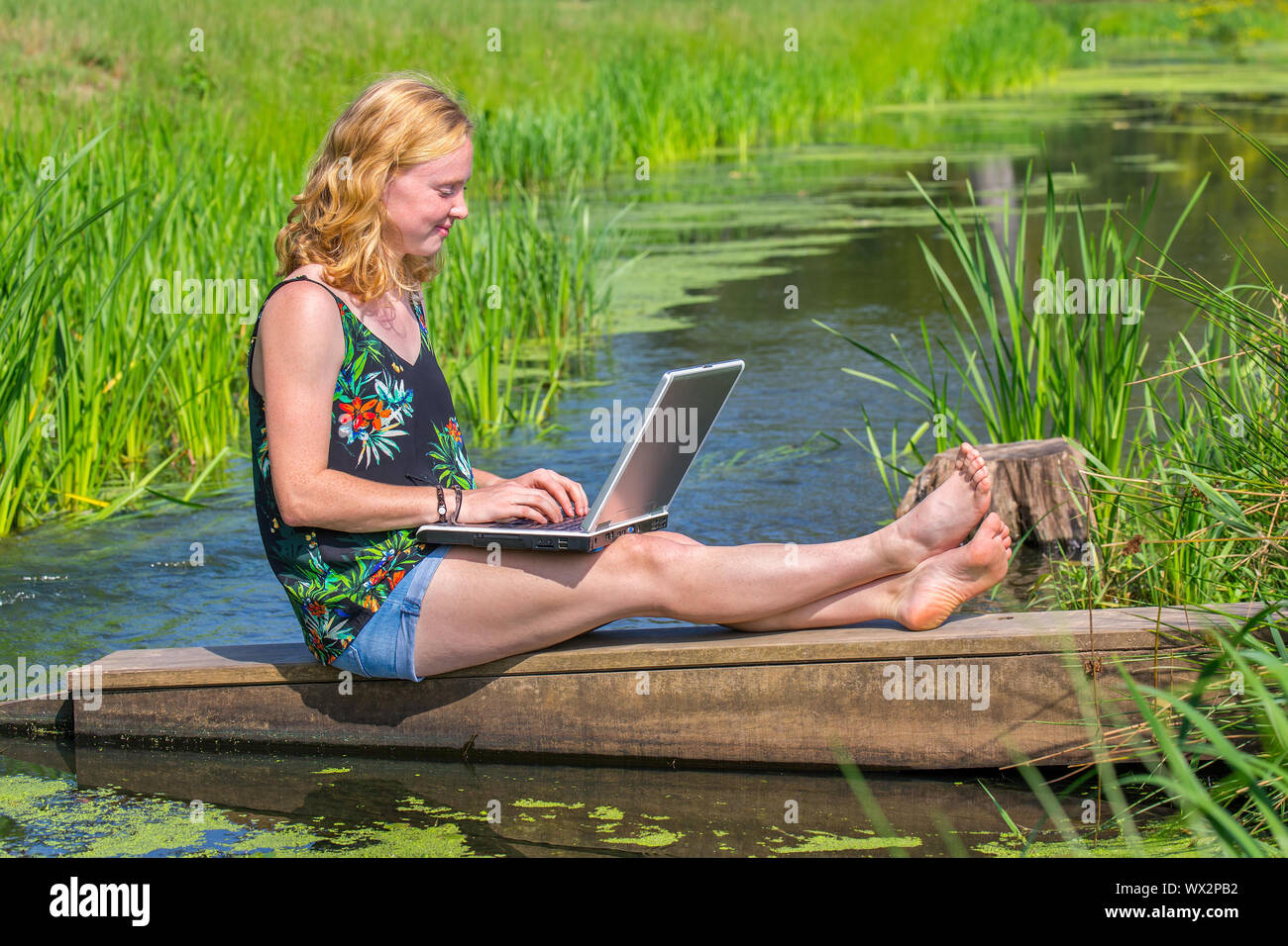 Young woman operating laptop near water in nature Stock Photo - Alamy