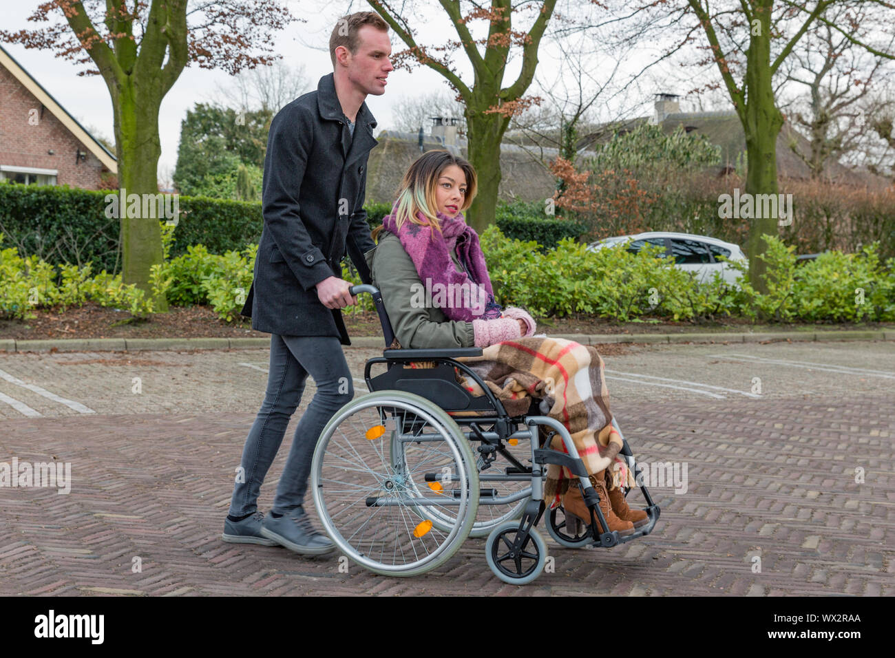 Man pushing a woman in a wheelchair at a parking place in a Dutch ...