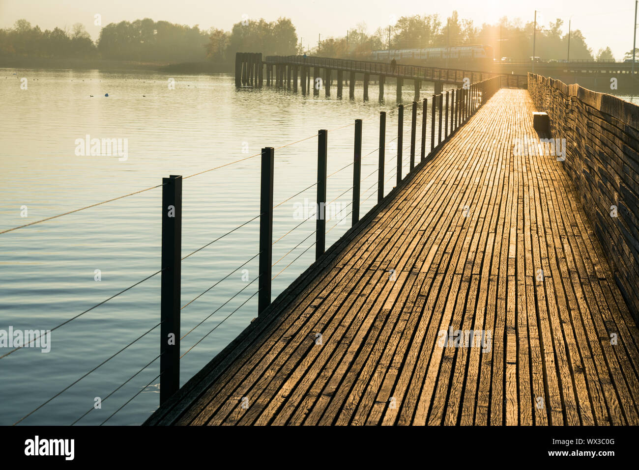 long wooden boardwalk pier over water in golden evening light with a ...