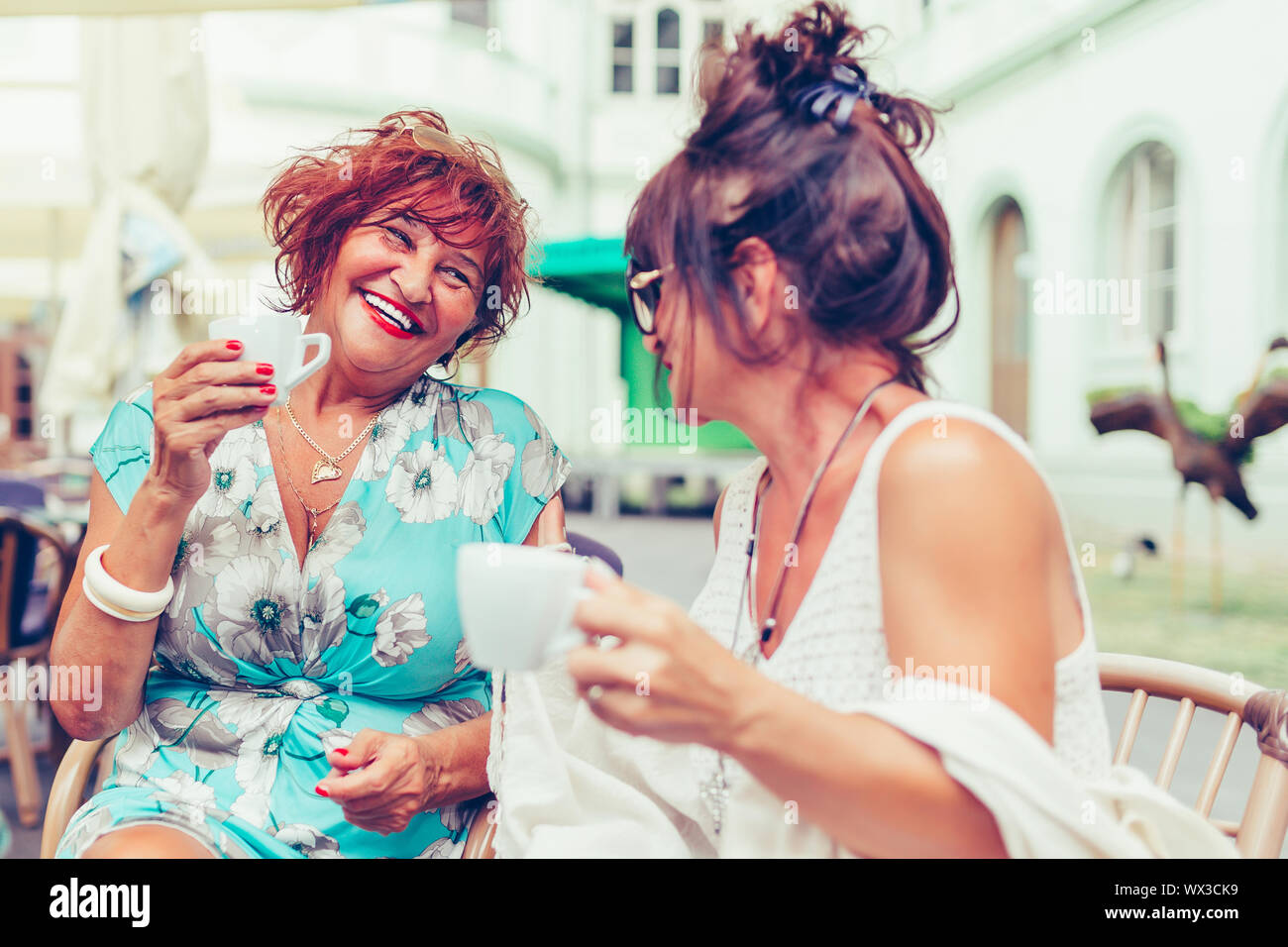 Two smiling senior women talking and drinking coffee while looking each ...