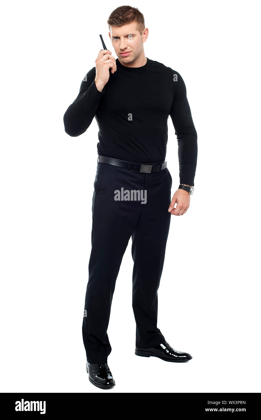 Full length portrait of male bodyguard communicating via walkie-talkie ...