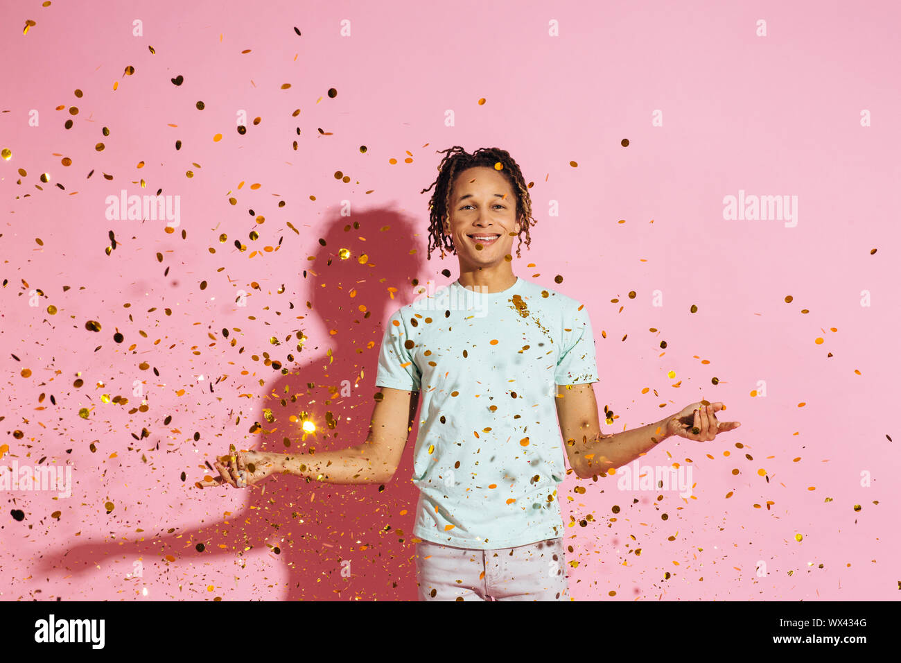 Smiling young man throwing gold confetti Stock Photo - Alamy