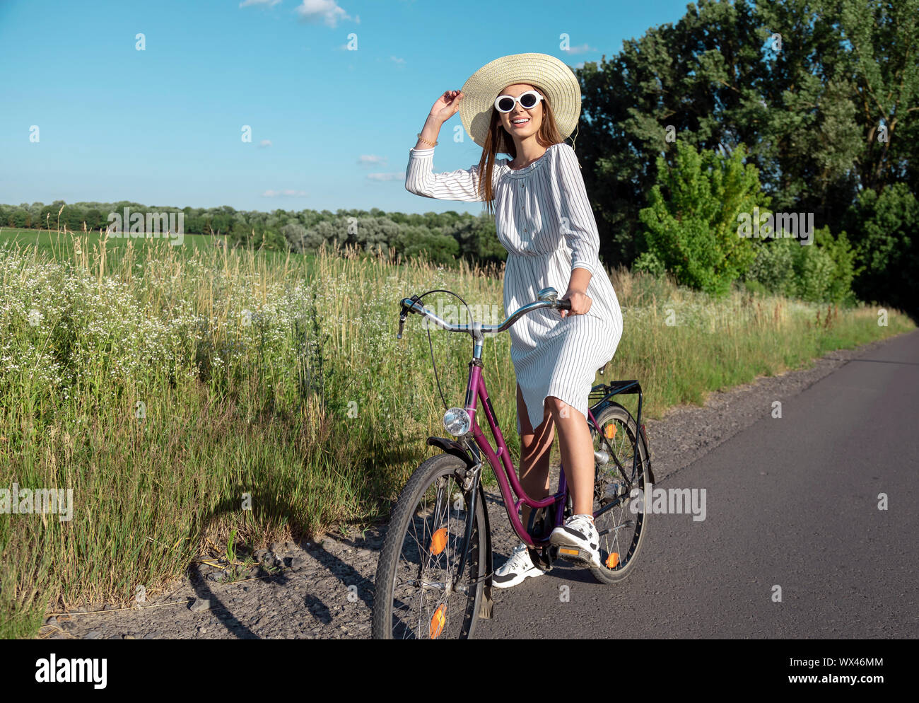 Cute cyclist girl adjusting her hat while having a rest on the roadside ...