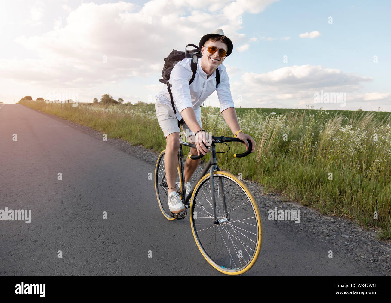 Cycling male tourist smiles at camera while riding along a rural road ...