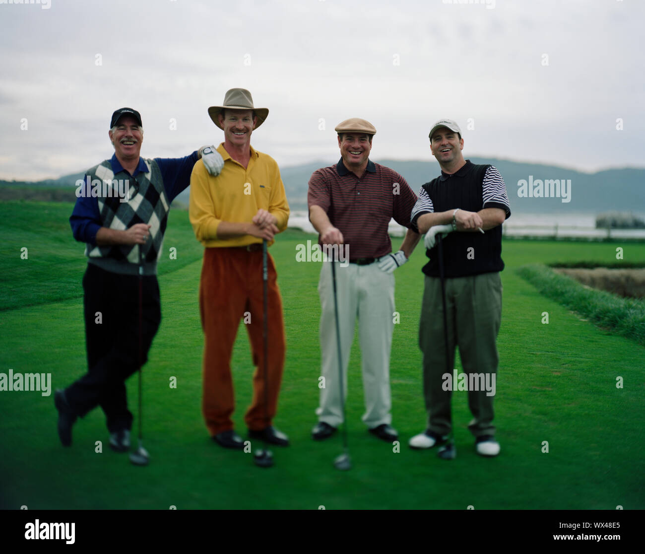 Portrait of four smiling men standing with golf clubs on a golfing ...