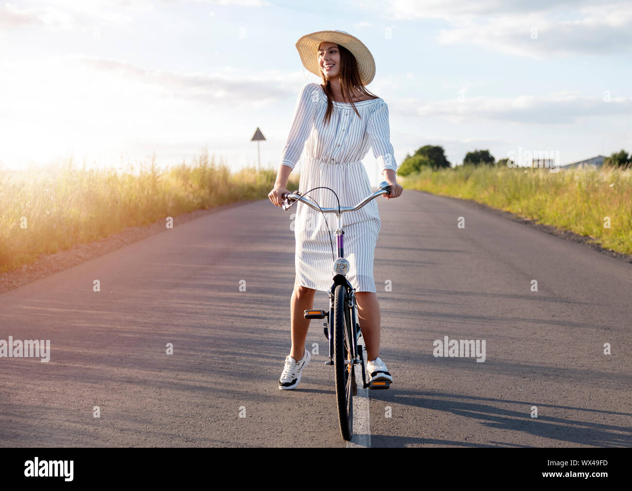 Pretty young cyclist girl has stopped amidst rural road to admire the ...