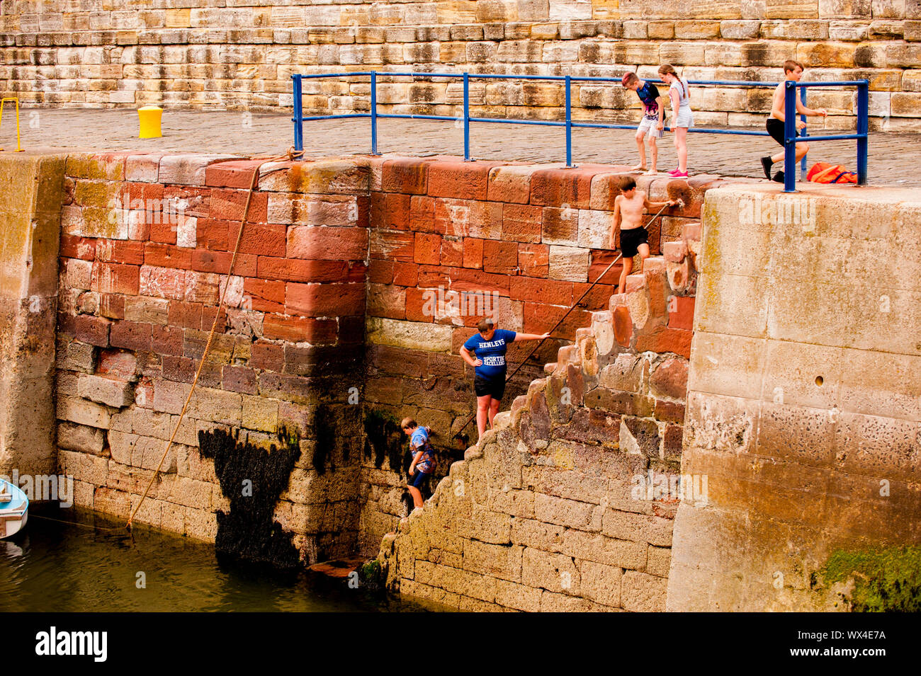 Kids playing in Dunbar harbour in a summer daily scene. Dunbar is a ...