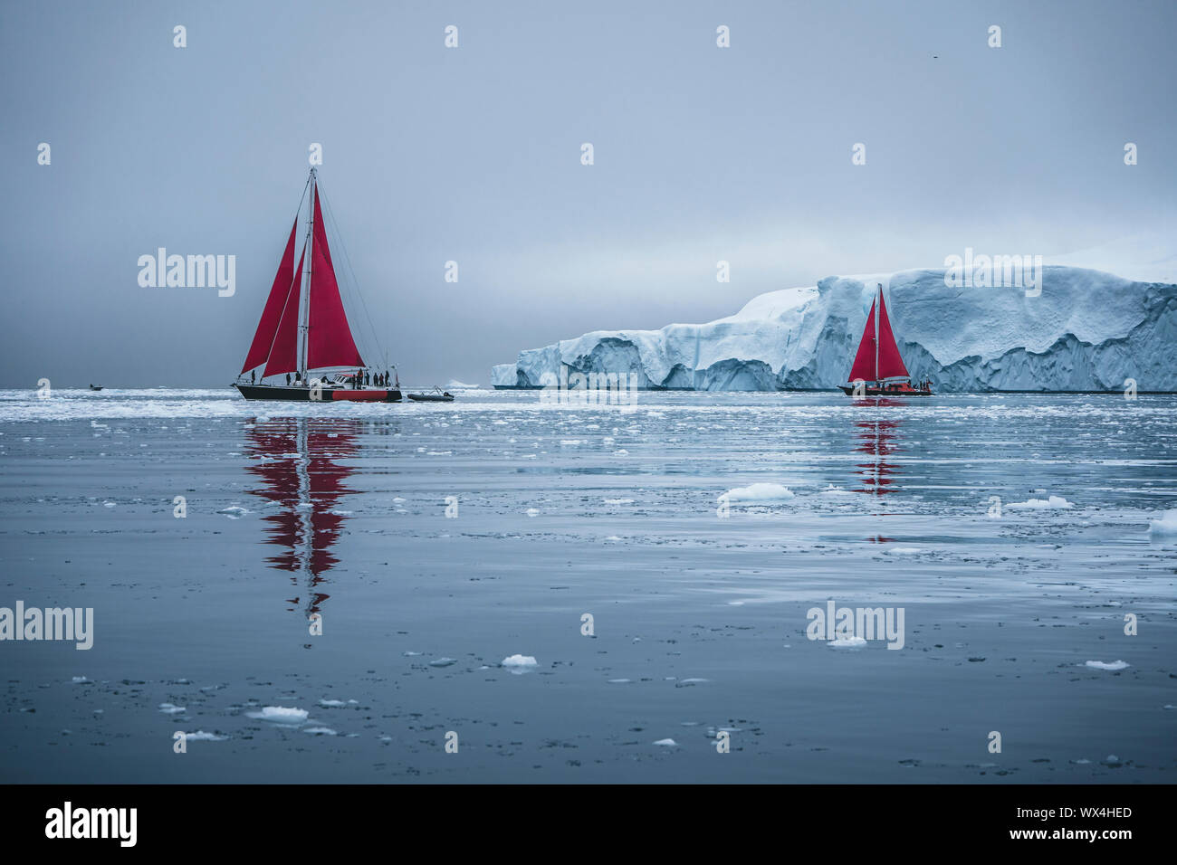 Beautiful red sailboat in the arctic next to a massive iceberg showing ...