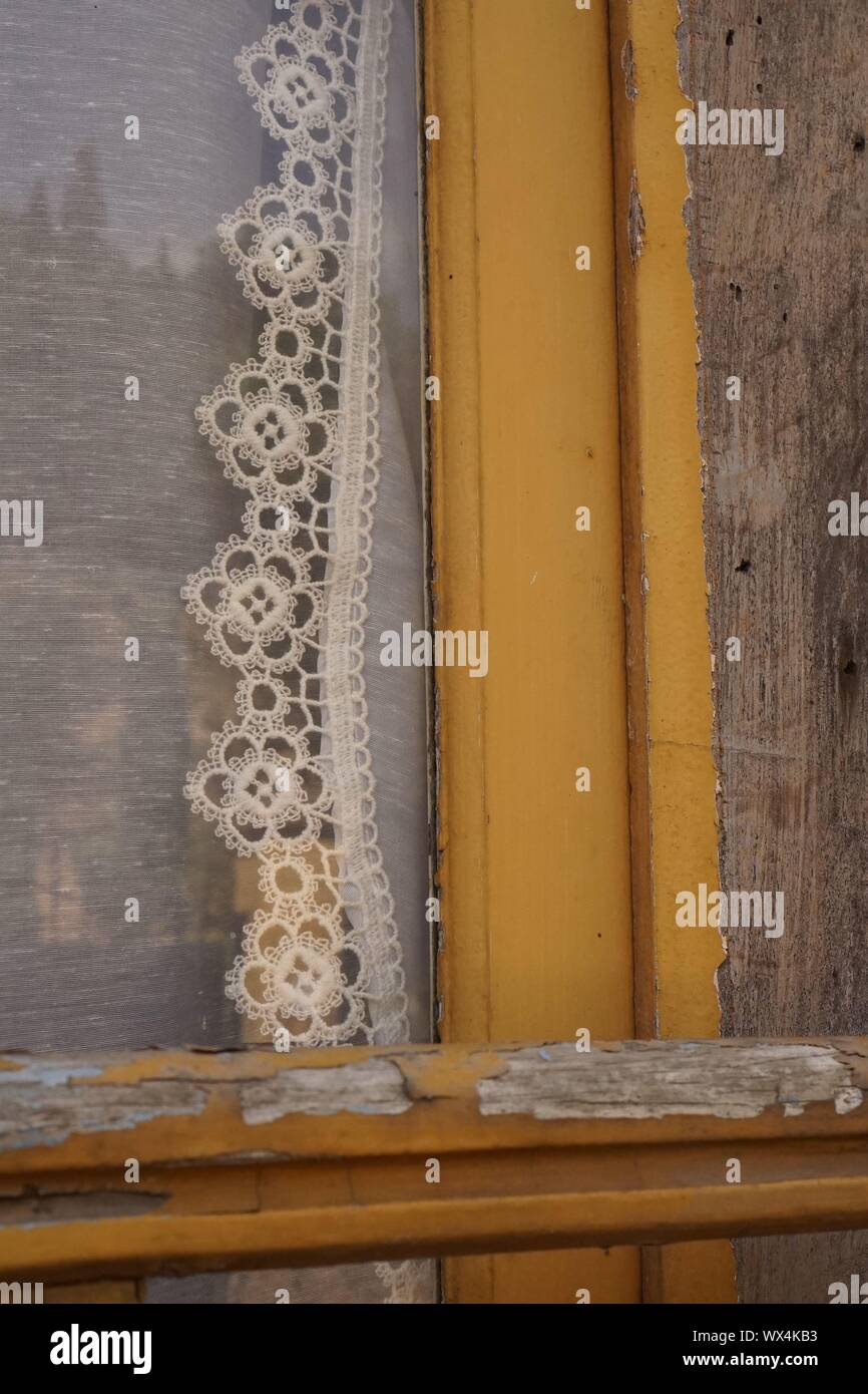 Close up of an old yellow wooden window frame with lace net curtain ...